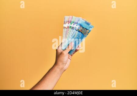 Hand of hispanic man holding canadian dollars over isolated yellow ...