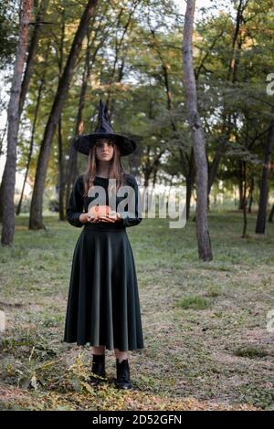 A woman in a witch costume in an orange hat holds a pumpkin lantern ...