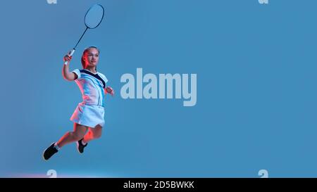 Motion. Beautiful dwarf woman practicing in badminton isolated on blue background in neon light ...