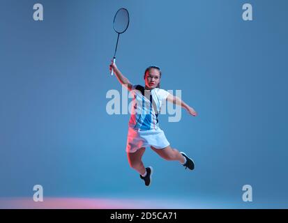 Strong. Beautiful dwarf woman practicing in badminton isolated on blue background in neon light ...