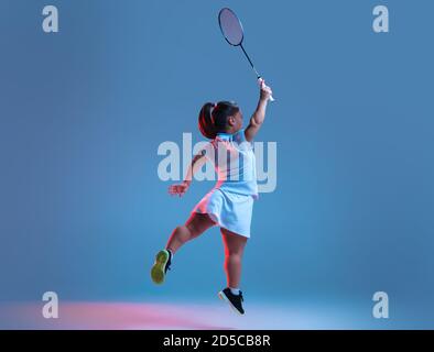 Strong. Beautiful dwarf woman practicing in badminton isolated on blue background in neon light ...