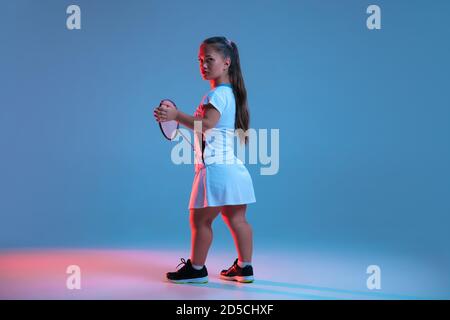 Dynamic. Beautiful dwarf woman practicing in badminton isolated on blue background in neon light ...