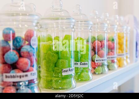 Labelled glass jars of green, yellow, red and blue sweets on a white ...