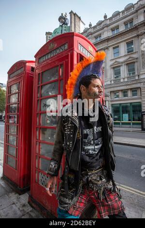 Punk rocker with mohican hair sits relaxing on top of red telephone ...