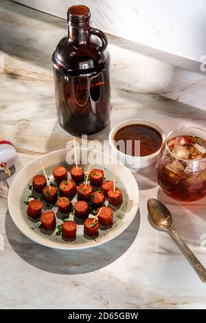 Cocktail hot dogs served with bourbon dipping sauce with glass of ...