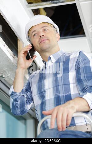 Portrait of young handyman making call while standing at construction ...