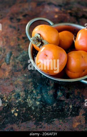 Group of persimmons in metal collander over rustic surface Stock Photo ...