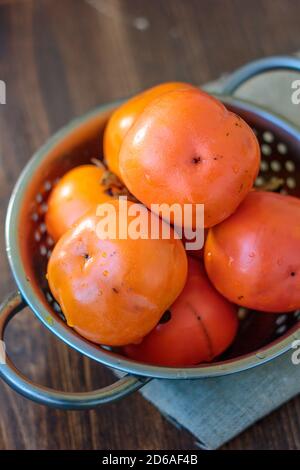 Persimmons in metal collander on wooden table Stock Photo - Alamy