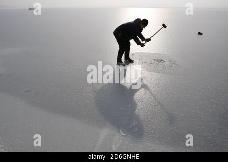 Fisherman breaking ice on surface of the frozen lake Stock Photo - Alamy