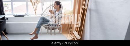panoramic crop of barefoot woman sitting near trash bin with recycle ...