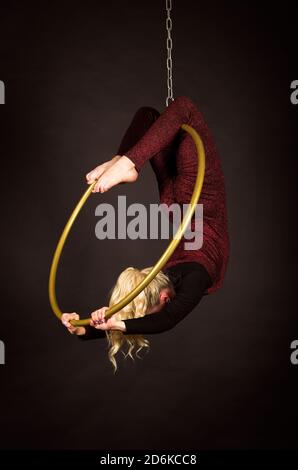Aerial performer in a gold costume suspended against a vibrant sunset ...