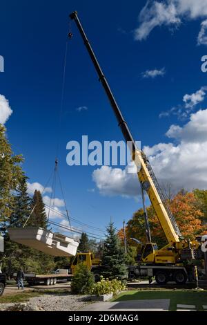 Crane lifting a fiberglass swimming pool shell into a hole dug in the ...