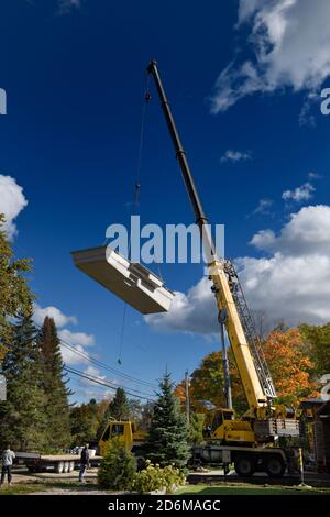 Crane lifting a fiberglass swimming pool shell into a hole dug in the ...