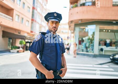 young handsome hispanic policeman wearing police uniform. Standing with ...