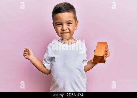 Adorable latin toddler holding gold ingot pointing thumb up to the side ...