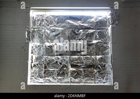 Tinfoil is taped over a window to block light from entering a room ...