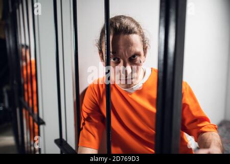 Harsh wild prisoner criminal maniac with tattoos grabs the bars. A ...