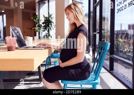 Pregnant businesswoman working with modern laptop at workplace in ...
