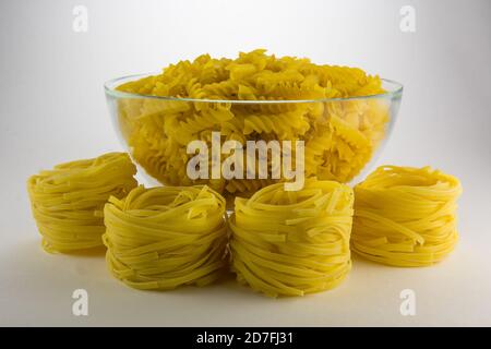 Fusilli in a deep glass plate and fettuccine on a white background ...