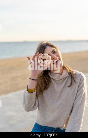 Beautiful caucasian woman holding donut pointing thumb up to the side ...