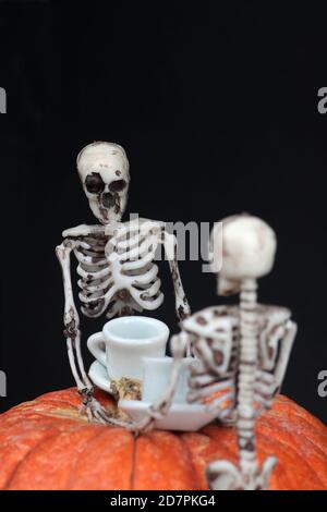 halloween concept - two skeletons drinking tea on pumpkin table against ...