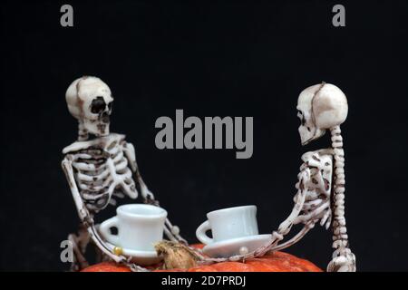 halloween concept - two skeletons drinking tea on pumpkin table against ...