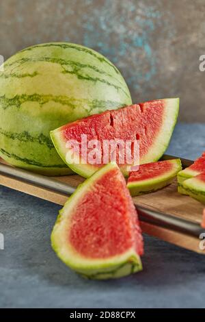 Mini Watermelon with sliced wedges on a wooden stand on a blue ...