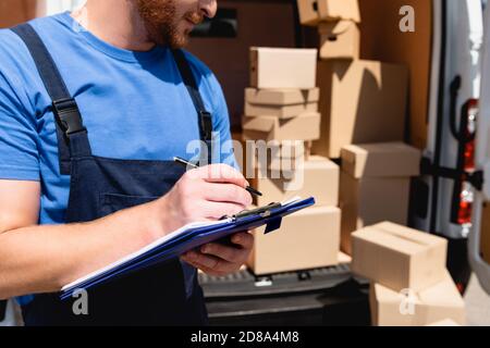 Loader in overalls holding clipboard near truck with packages outdoors ...