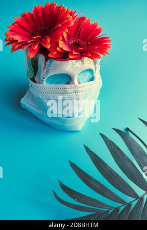 Skull in face mask with coral color gerbera flowers. Dia de los Muertos ...