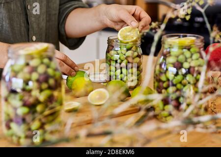 Woman prepares fermented olives in glass jars in the kitchen. Autumn ...