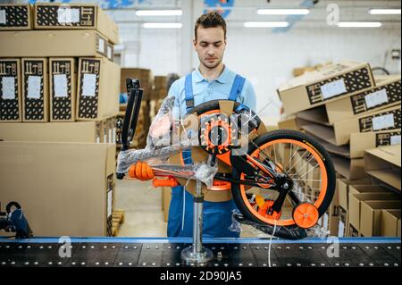 Bicycle factory, worker packs teen bike. Male mechanic in uniform ...