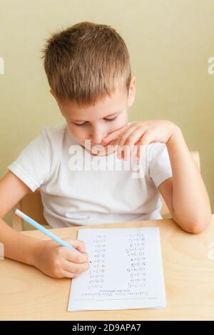 Cute 7 years old child doing his homework sitting by desk. Boy writing ...