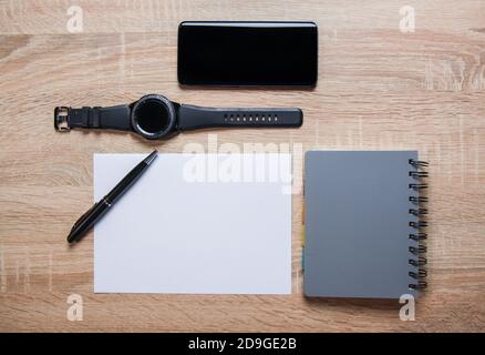 Smartphone and smartwatch next to a notebook and blank card on a wooden ...