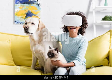 Frightened African American girl with VR glasses on eyes smiling leans ...