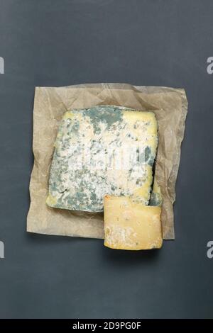 Several pieces of spoiled cheese on a white plate on a gray background ...