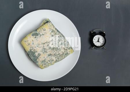 Several pieces of spoiled cheese with a clock on a white plate on a ...