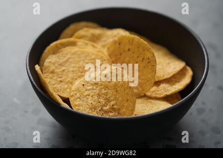 Round nachos in black ceramic bowl on concrete background, shallow ...