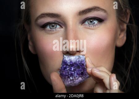 Young beautiful woman holding amethyst gemstone over isolated pink ...
