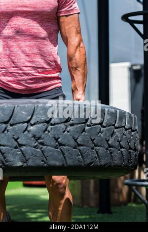 Muscular focused male athlete lifting heavy tire during active ...