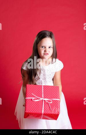 unhappy kid with curly hair in puffer jacket and hat. teen girl on red ...