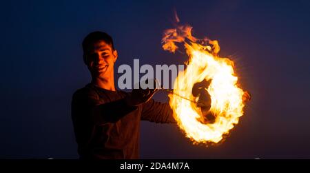 Happy guy artist perform fire circle by spinning burning poi on idyllic ...