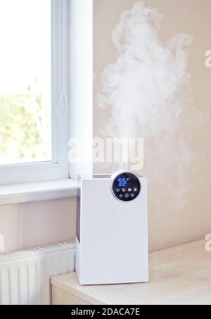 Modern air purifier and table near light wall in bedroom Stock Photo ...