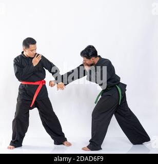 two Asian men wearing pencak silat uniforms fight with tendangan lurus ...