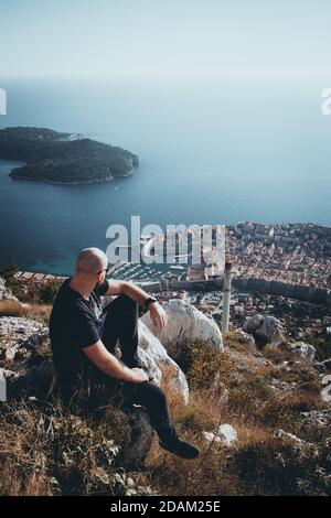 A vertical aerial shot of a man on the peak of the mountain looking at ...