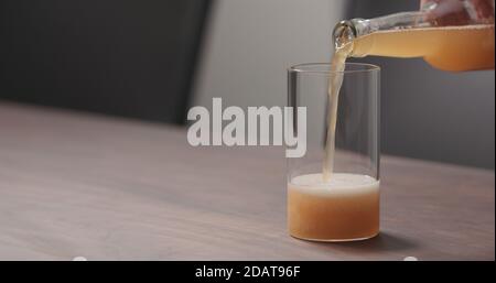 Slow motion pour orange soft drink into highball glass on walnut table ...
