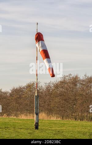 A windsock in red and white stripes in a hanging position at a lamppost ...