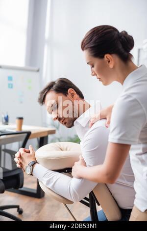 Masseuse doing shoulder massage on young woman on massage table in ...