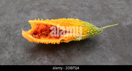 Orange bitter gourd, with ridged flesh, split open to show red seeds ...