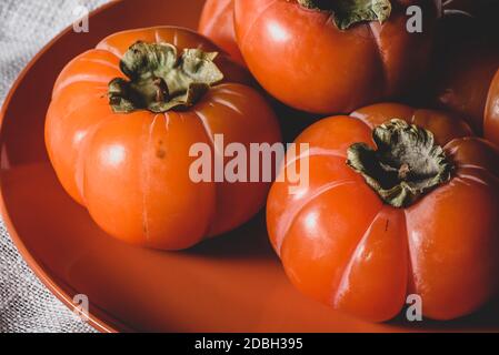 Few fresh persimmons on orange plate over white textile Stock Photo - Alamy