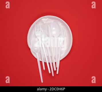 round plate and stack of plastic forks and spoons on red background ...